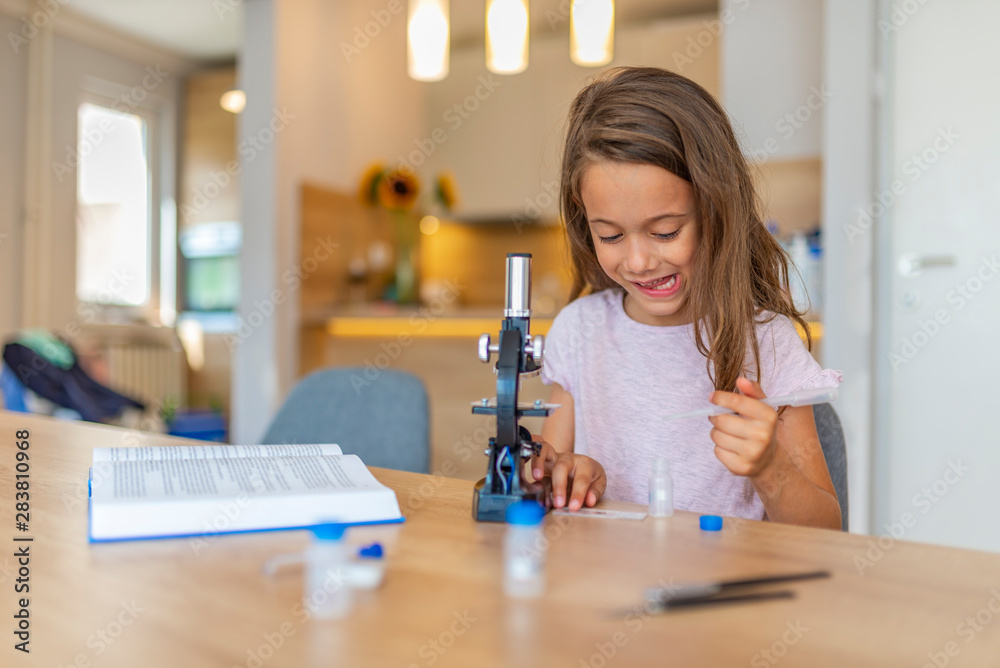 Little girl concentrates while using microscope. Studying chemistry ...