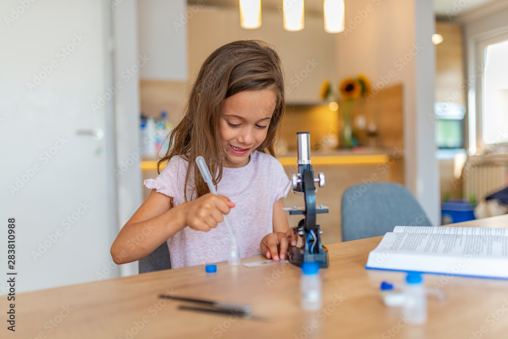 Little girl concentrates while using microscope. Studying chemistry ...