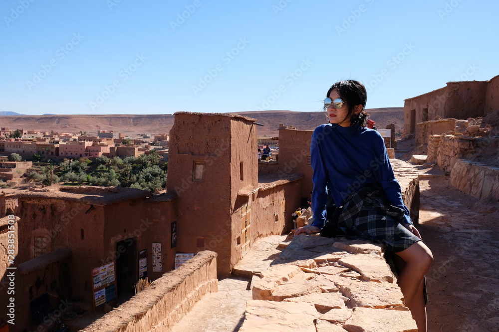 One young Asian girl sitting on old brown city wall of Ait Ben Haddou ...