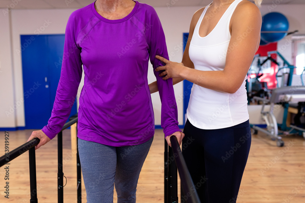 Female physiotherapist helping disabled senior woman walk with parallel ... Female physiotherapist helping disabled senior woman walk with parallel ...