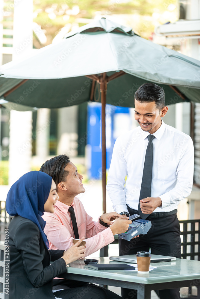 Waiter interacting with Muslim customers using bank terminal to process ...