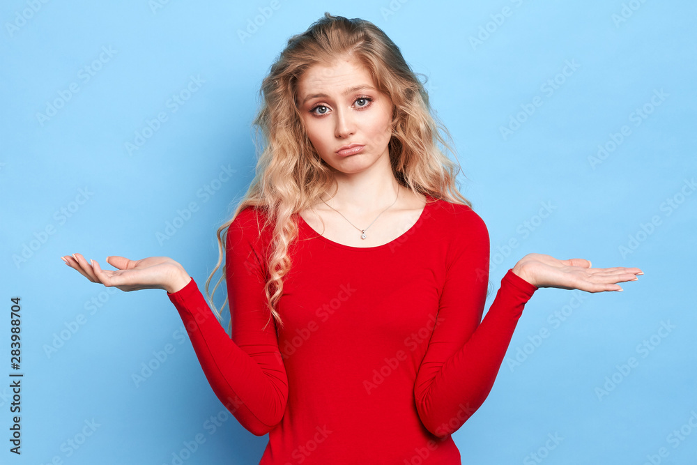 Puzzled hesitant girl with long fair hair dressed casually, shrugs ...