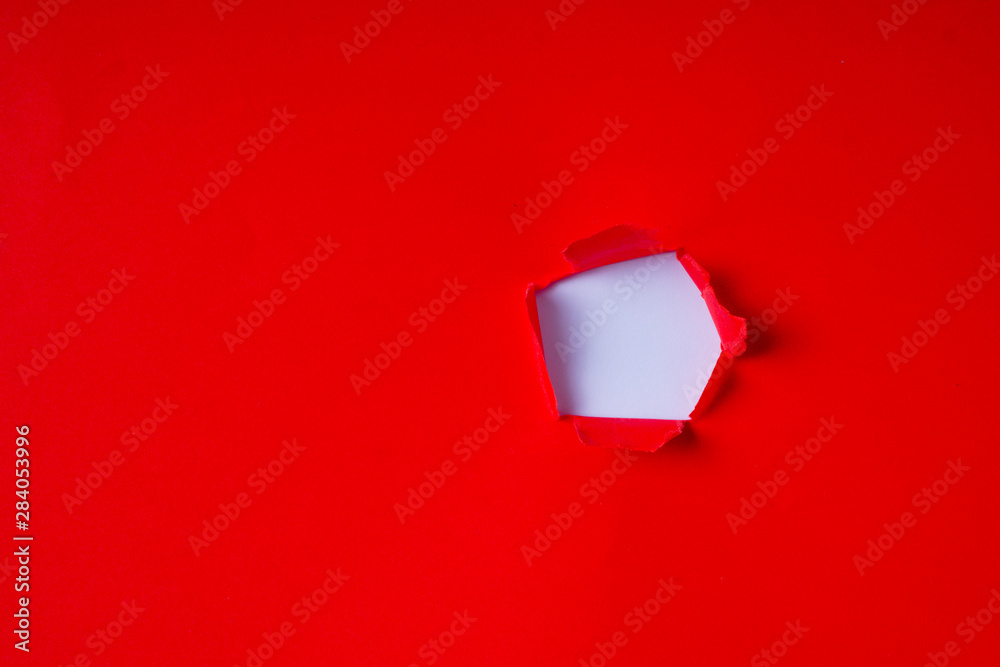 Torn red coloured paper on white background with closeup hole in the ...