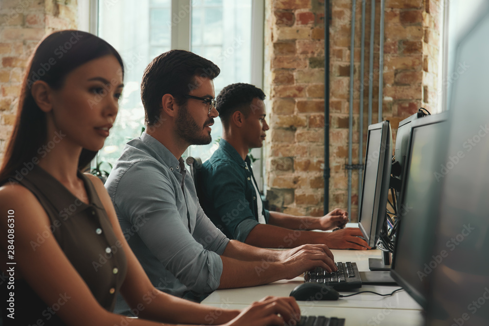 Office life. Side view of young employees working on computers while ...