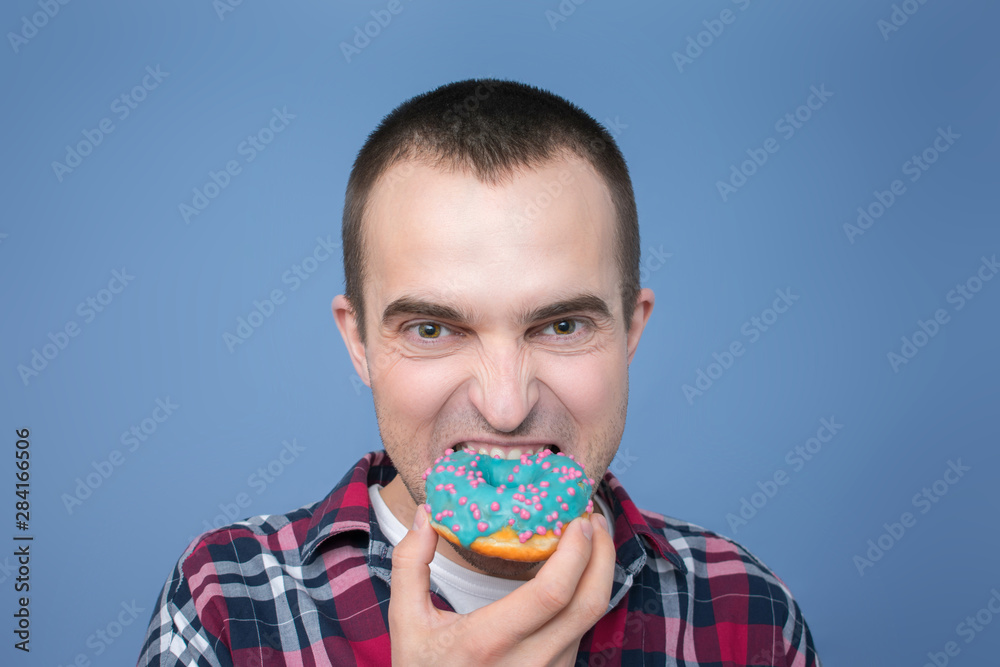 Hungry male eagerly taking a bite of blue donut with bright sprinkles ...