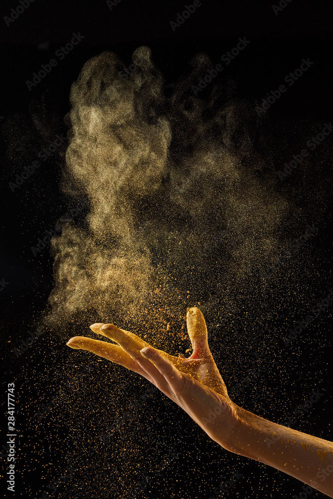Woman's hand scatters gold dust on a black background with copy space ...