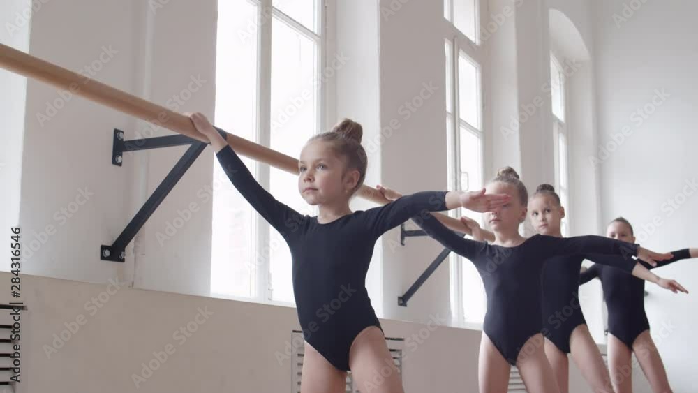 Female ballet teacher helping four little Caucasian girls wearing black ...
