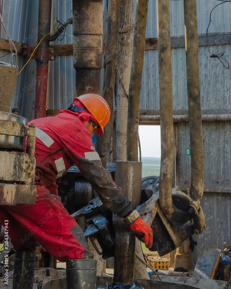 Work driller in red uniform, in helmet and goggles. He with the help of ...
