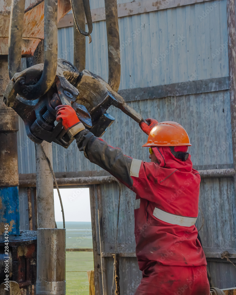 Work driller in red uniform, in helmet and goggles. He with the help of ...