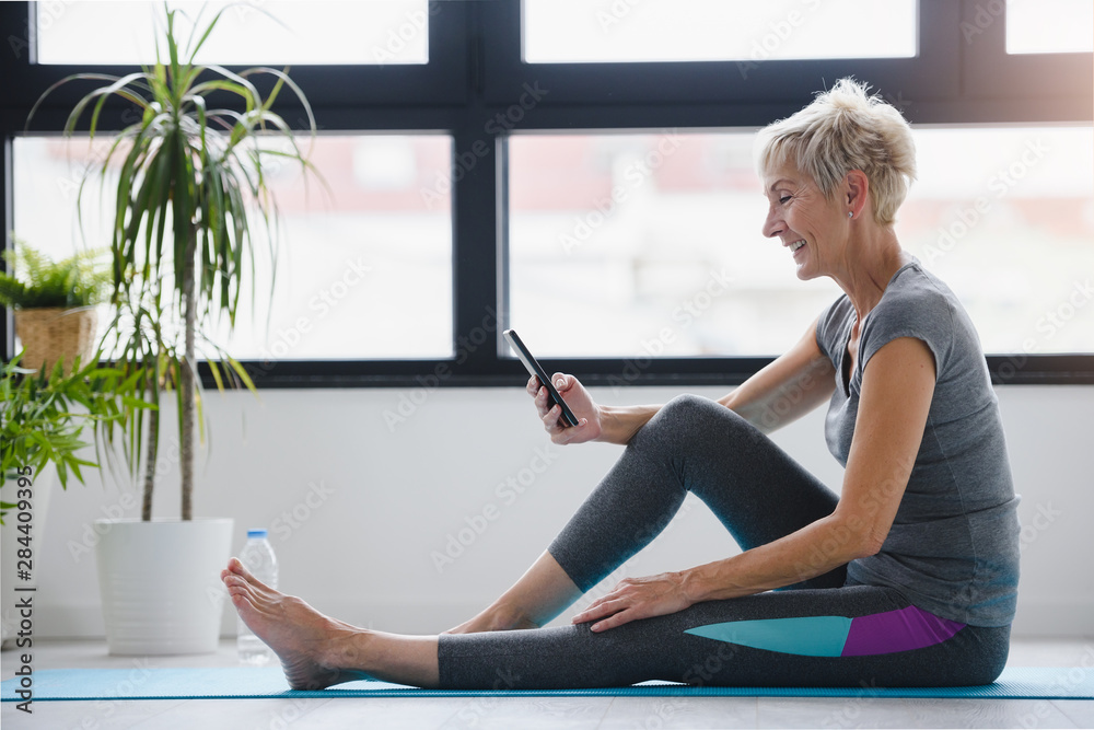 Senior woman using smartphone at home after exercise. The use of ...
