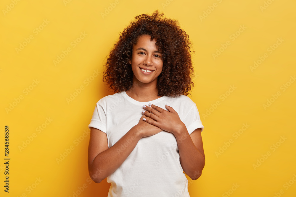Pretty young Afro American female keeps palms near heart, expresses ...