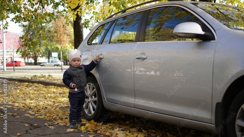 Cute little boy standing near the grey car on a city street in autumn ...