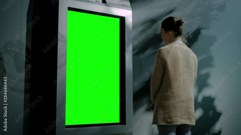Woman looking at vertical blank digital interactive green display kiosk ...