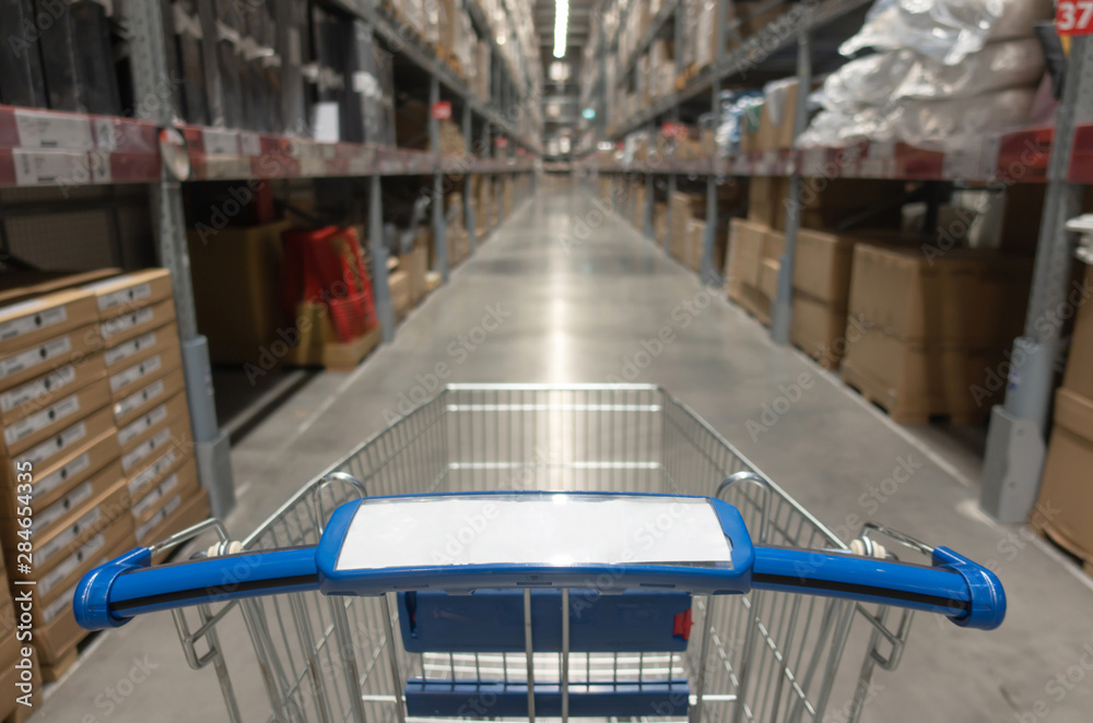 blue shopping cart with blurred view of warehouse interior with product ...
