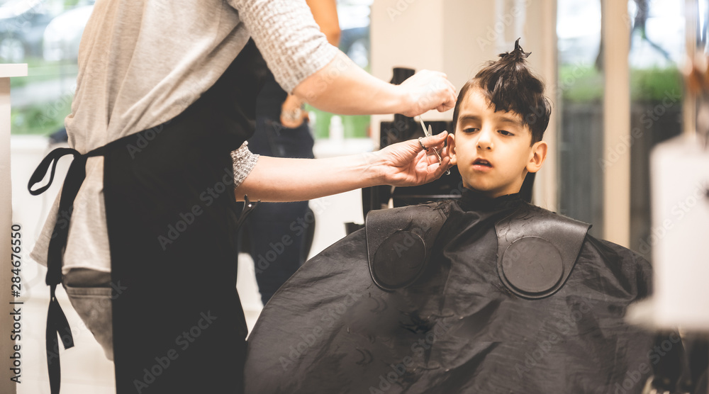 Hairdressers hands making hairstyle to child little boy in the barber ...