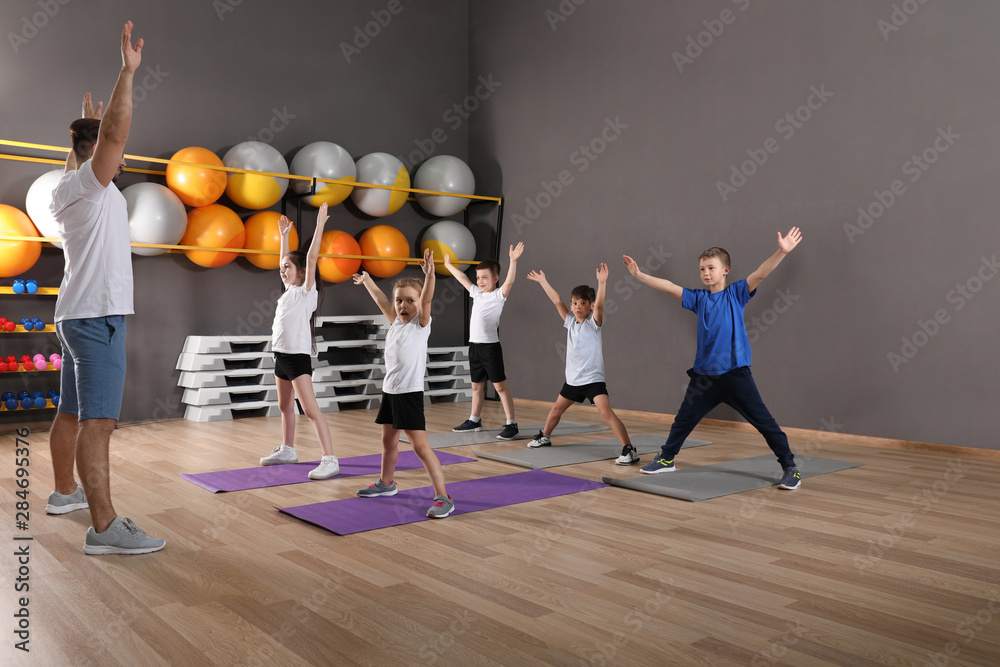 Cute little children and trainer doing physical exercise in school gym ...