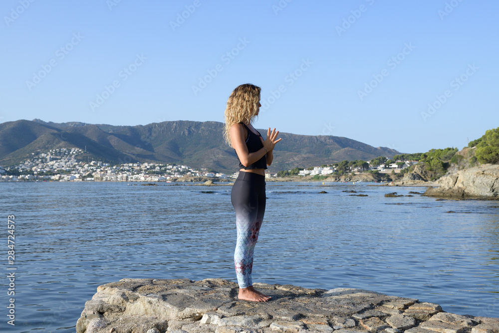 Young girl doing yoga on a small beach pier with a Mediterranean ...