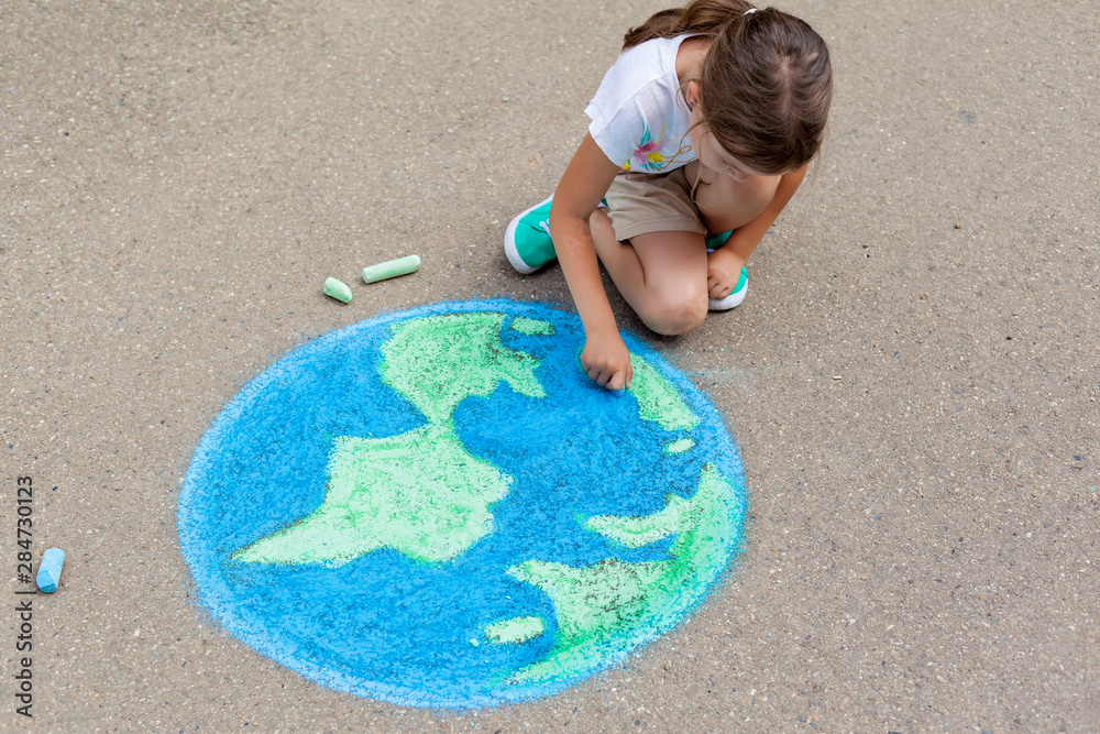 the child girl draws a planet of the world with colored chalk on the ...