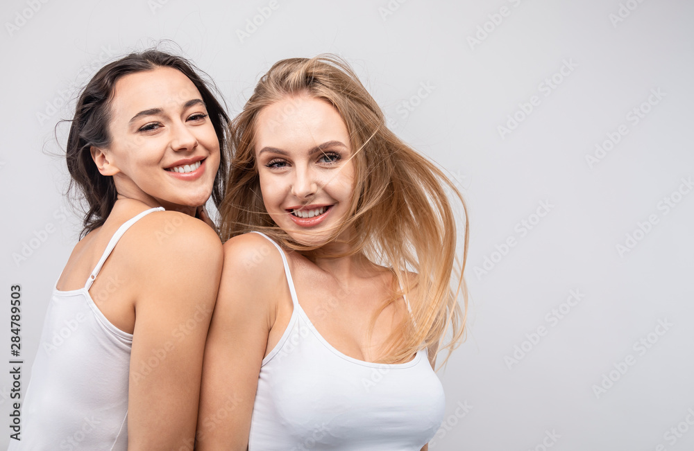 Smiling girls in white tank tops nestling each other looking at camera ...
