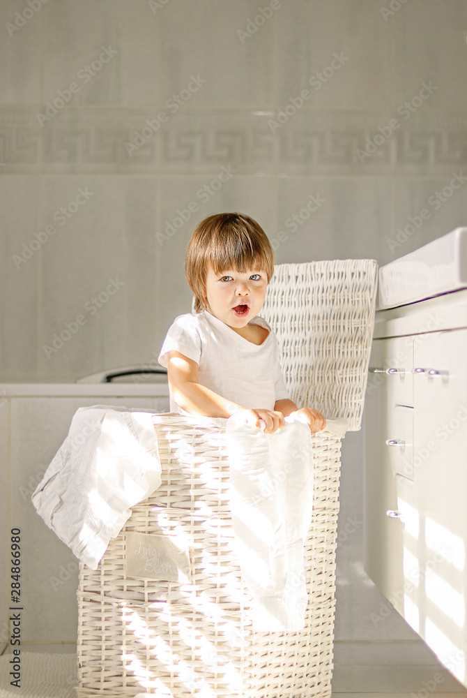 Cute little playful boy standing inside white wicker laundry basket ...