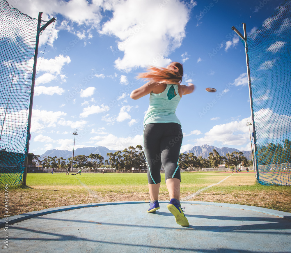 Wide angle action photo of a female discus athlete throwing a discus ...