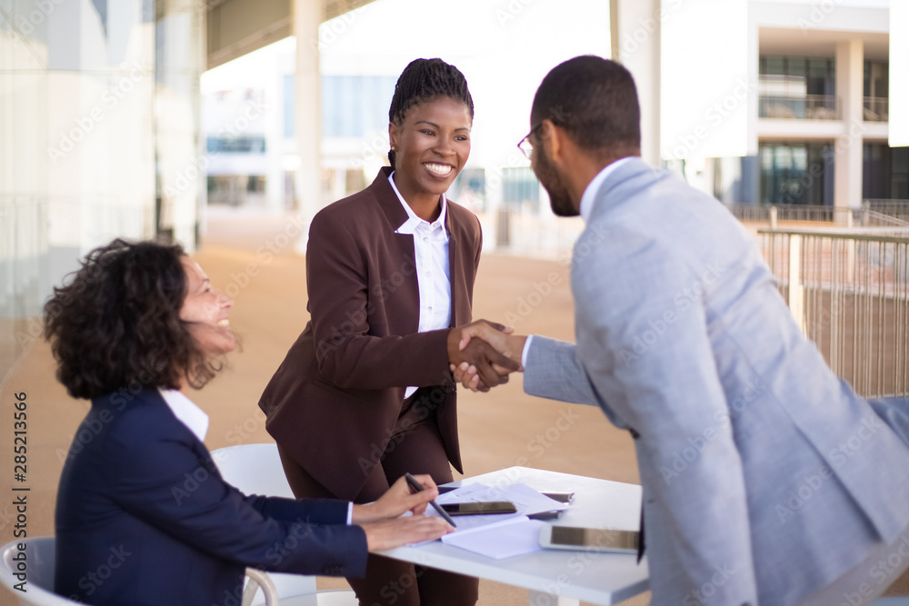 Happy sales agent welcoming customer in outdoor cafe. Business man and ...