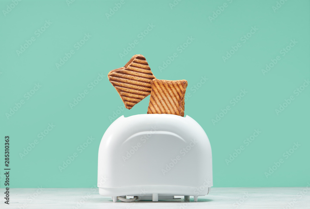 Roasted toast bread popping up of toaster with green wall, front view ...