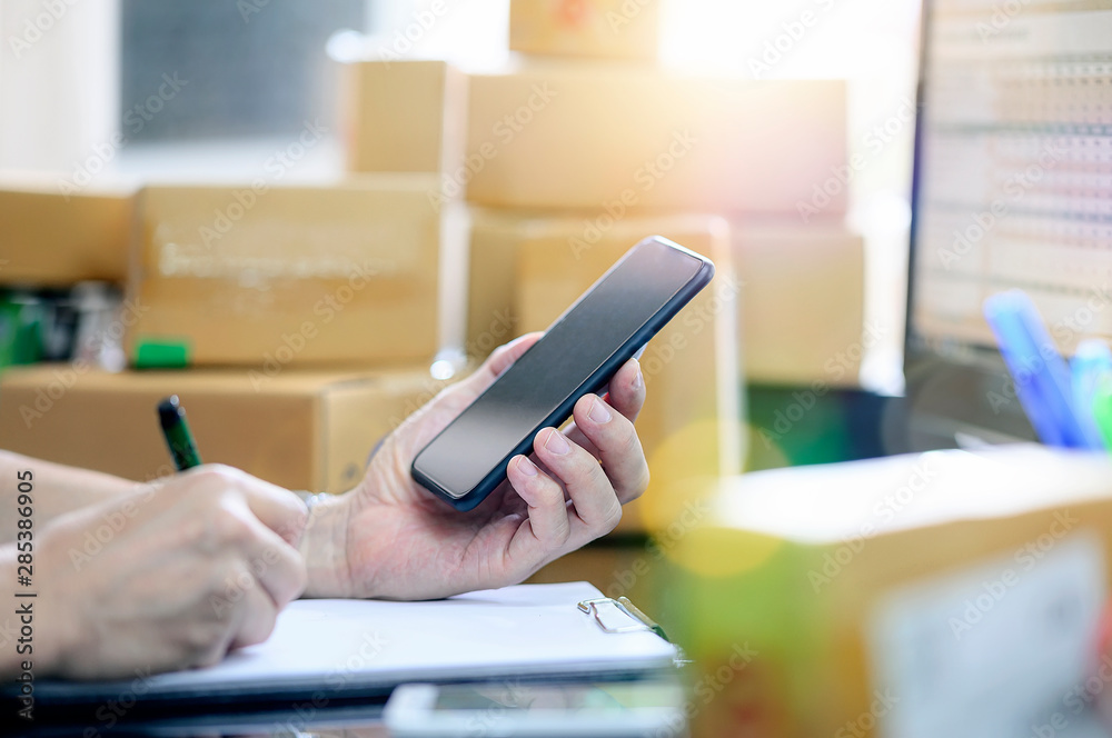 Cropped short of man checking purchase order in mobile phone and write ...