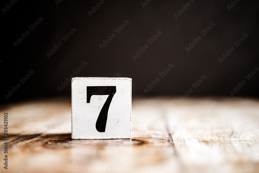 7 - Number 7 - Number Seven - White block with number on wooden table ...
