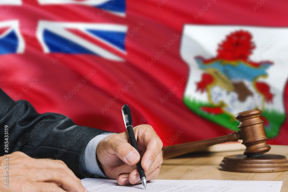 Judge writing on paper in courtroom with Bermuda flag background ...