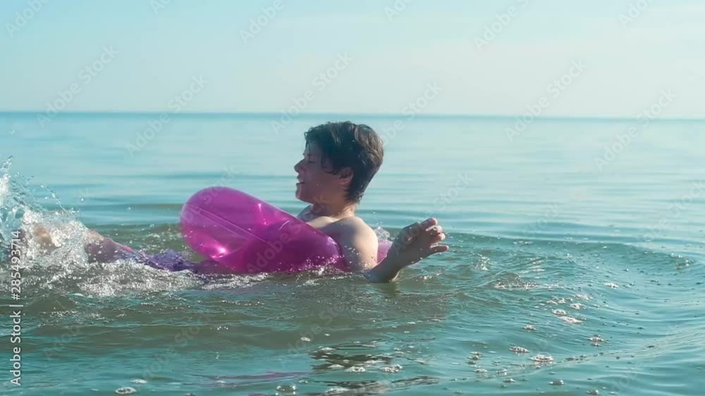 a young man swimming in the sea. floats on a pink inflatable circle ...