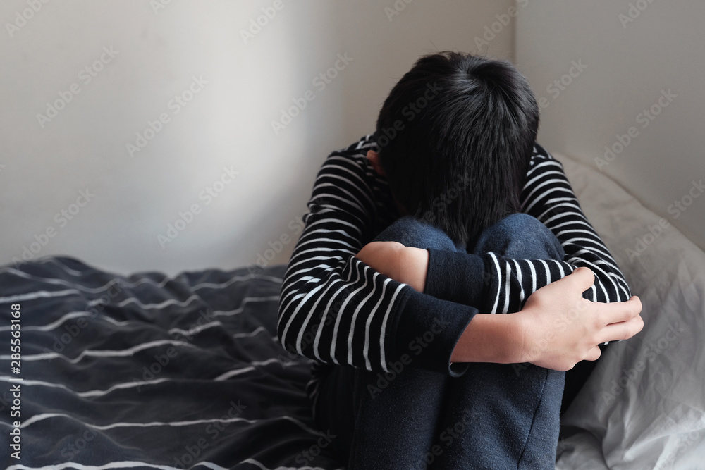 Depressed,despair young preteen teenage boy hugging his knee in bedroom ...