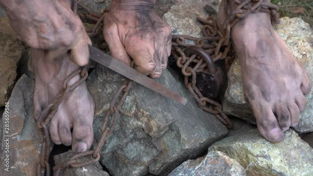 Hands and feet of a slave entangled in iron chains. An attempt to break ...