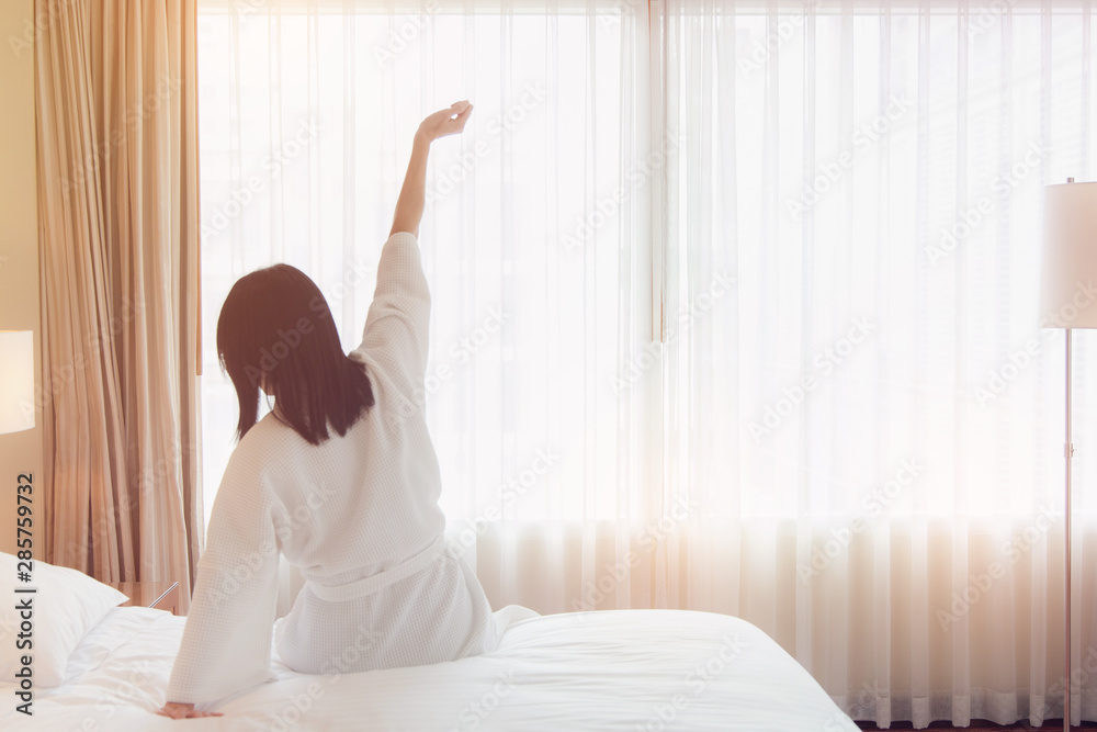 Woman stretching in bed after waking up, back view. Woman sitting near ...