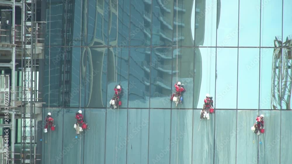 Group of workers cleaning the windows of a high rise building, dangling ...