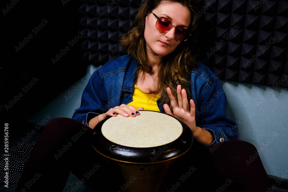 A young woman plays a drum djembe sitting on the floor in a recording ...