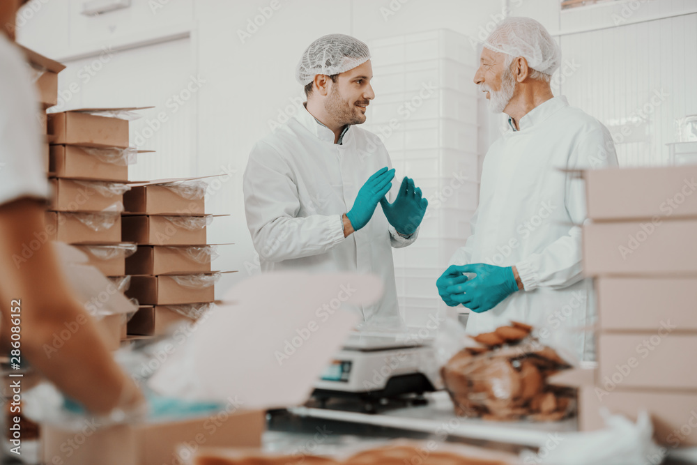 Younger employee explaining to his older colleague how to do packing ...