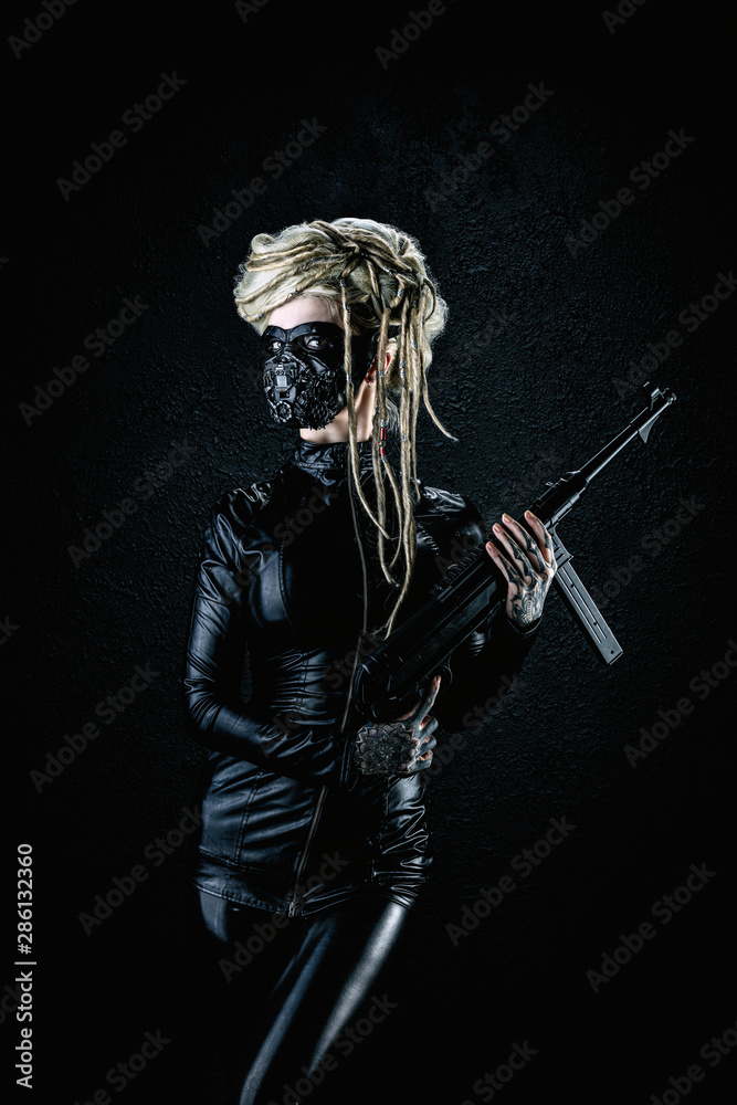 Young cyborg woman in leather suit and gas mask, holds in her hands a ...