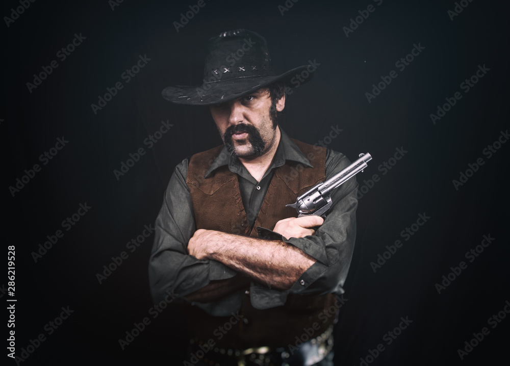 Foto de Cowboy standing with crossed arms, holding a revolver handgun ...