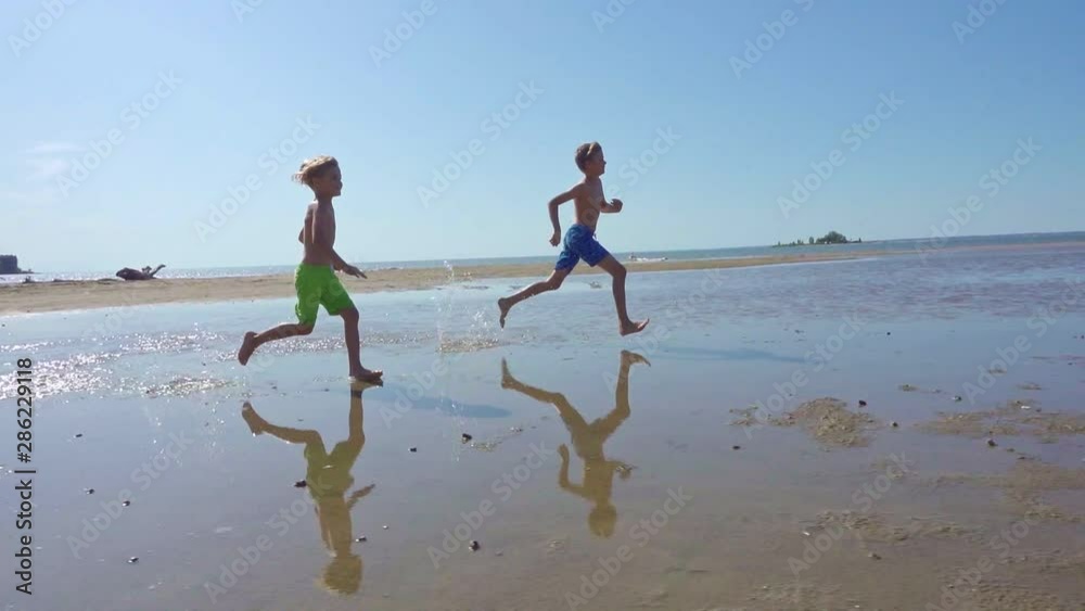 Slow motion of running boys in shallow sea water. Two of young children ...