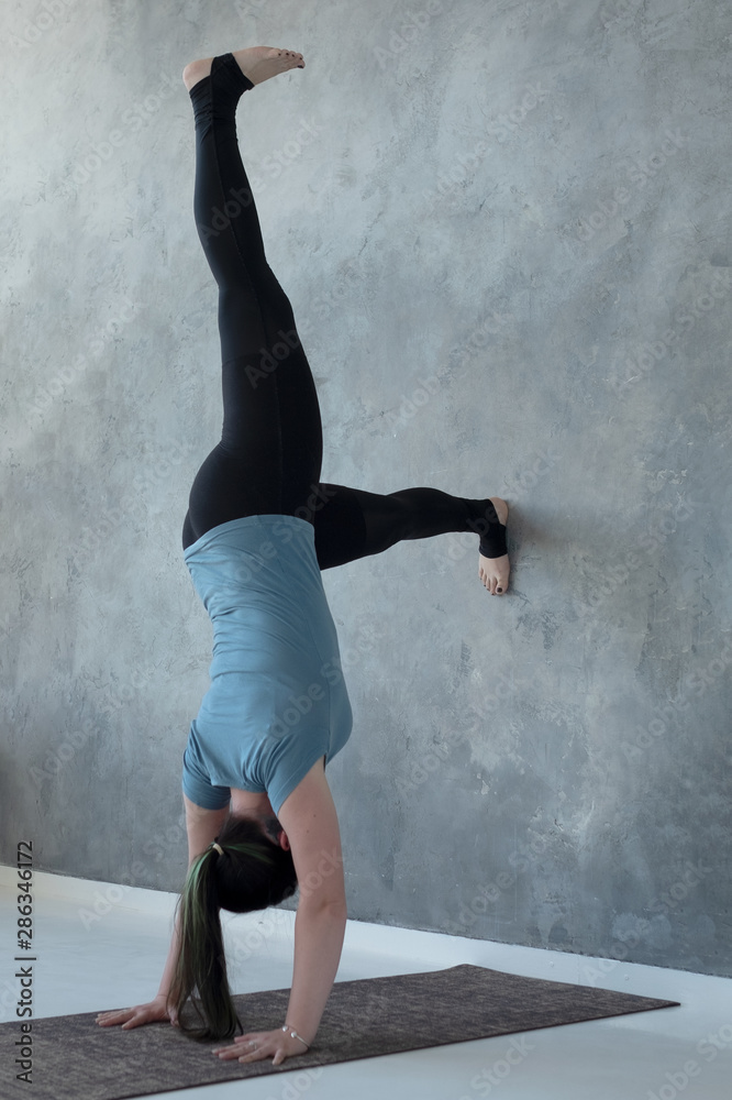 Woman learning to stand on hands near wall. Upside down yoga position ...