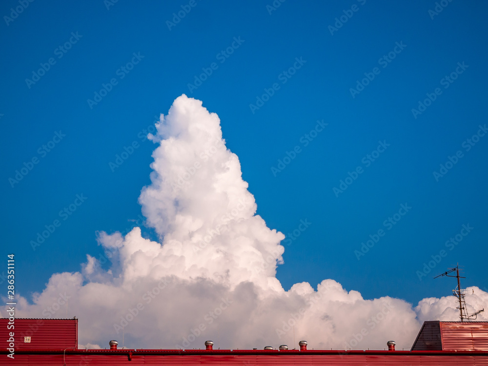 Massive cloud with spectacular shape rises high into the blue sky over ...