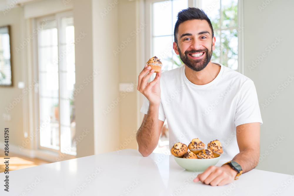 Handsome hispanic man eating chocolate chips muffin with a happy face ...
