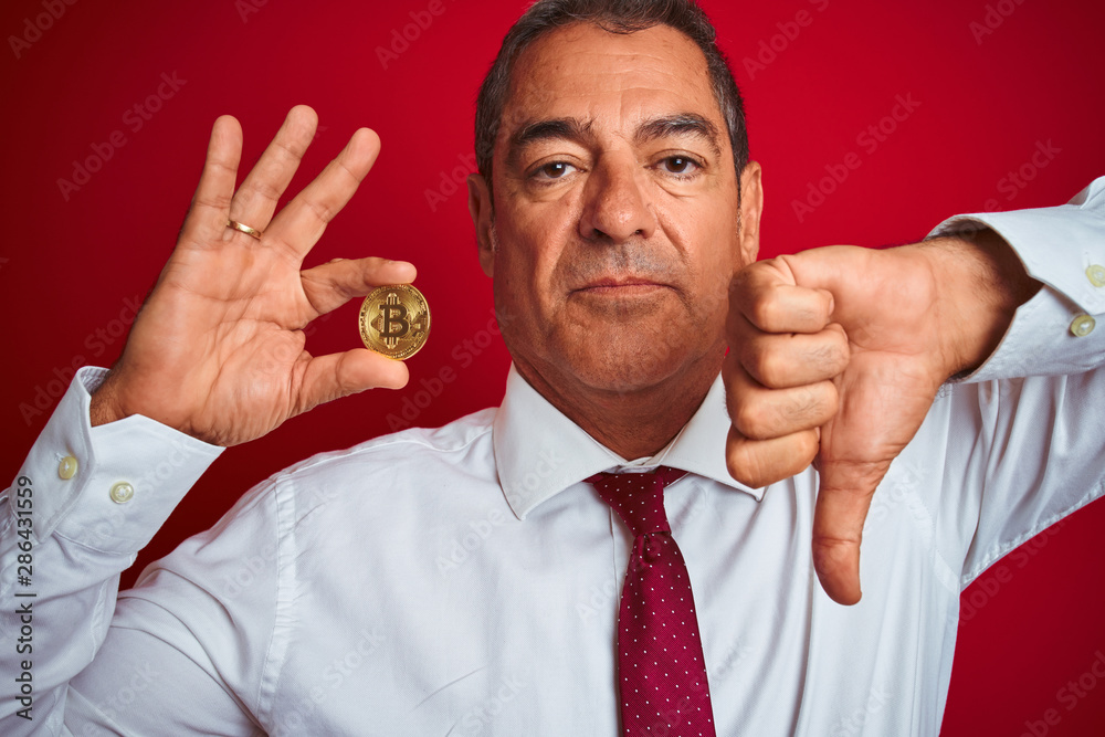 Handsome middle age man holding bitcoin standing over isolated red ...