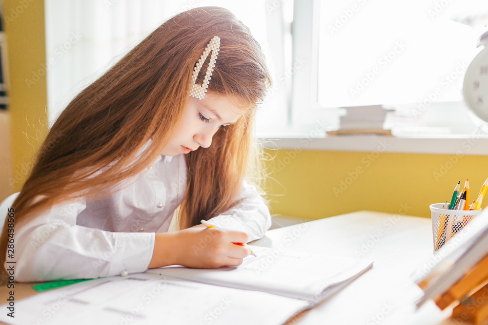 Education at home concept - Cute little girl with long hair studying or completing home work on ...