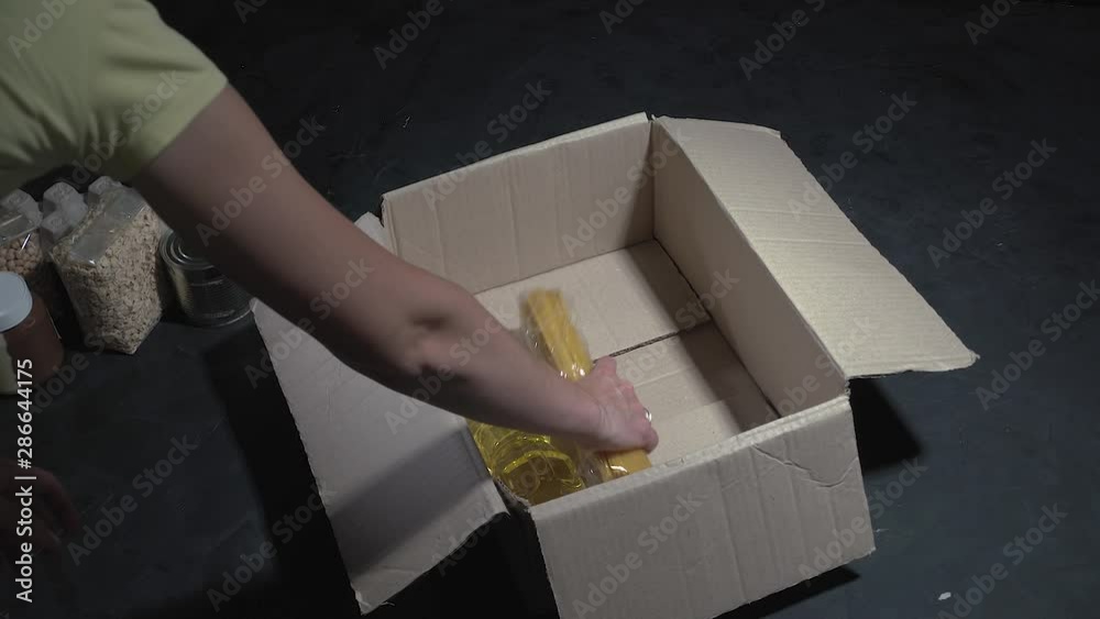 Female hands packing a box of different products on dark background ...