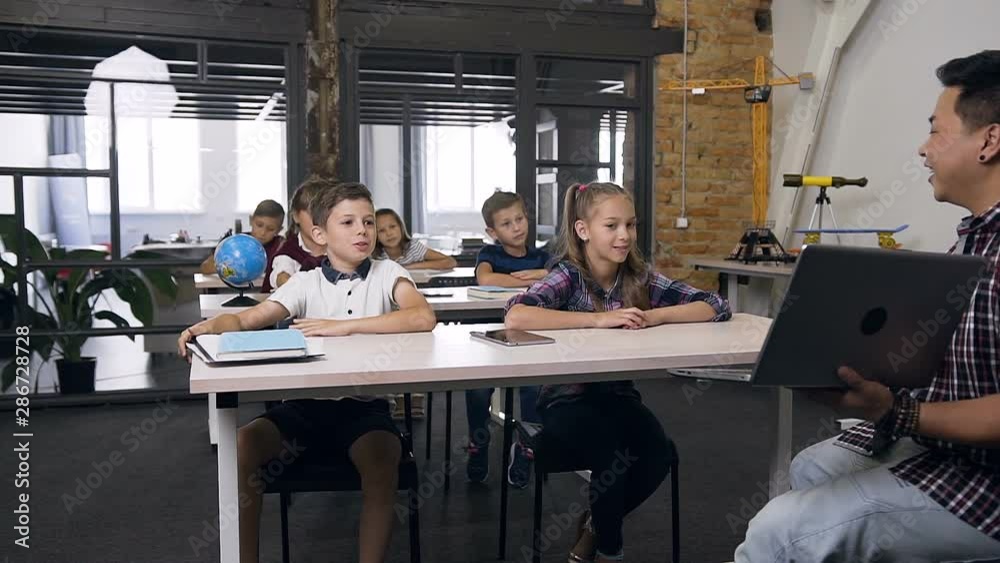 Cute caucasian boy sitting behind desk together with classmate, raising ...