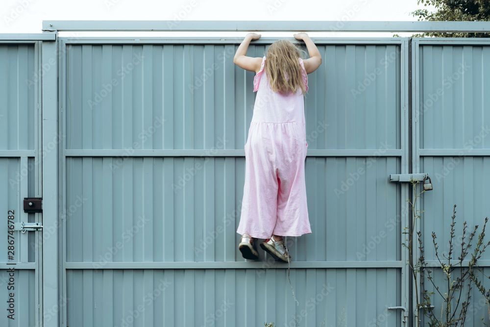 Girl climbing metal fence outdoor. Curious child on high white painted ...