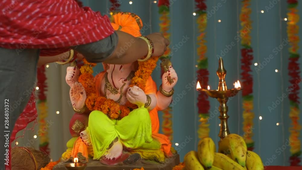 Overhead shot of an Indian female garlanding Lord Ganesha idol and ...