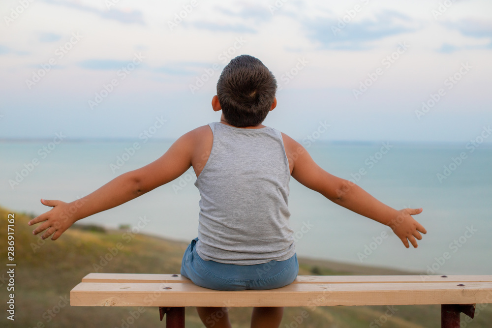 Boy spread his arms against the backdrop of the sun over the green ...